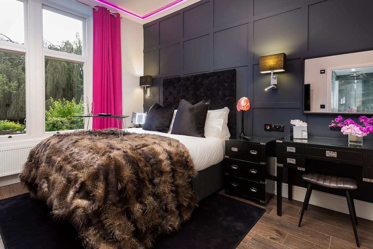 Quarto moderno com uma cama grande, uma penteadeira com espelho e vista para o verde lá fora.