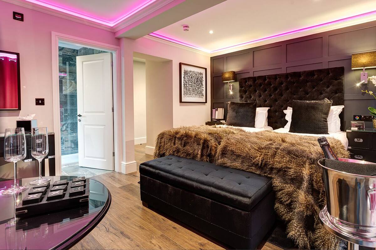 Quarto moderno com cama grande, mesa de centro de vidro e minibar.