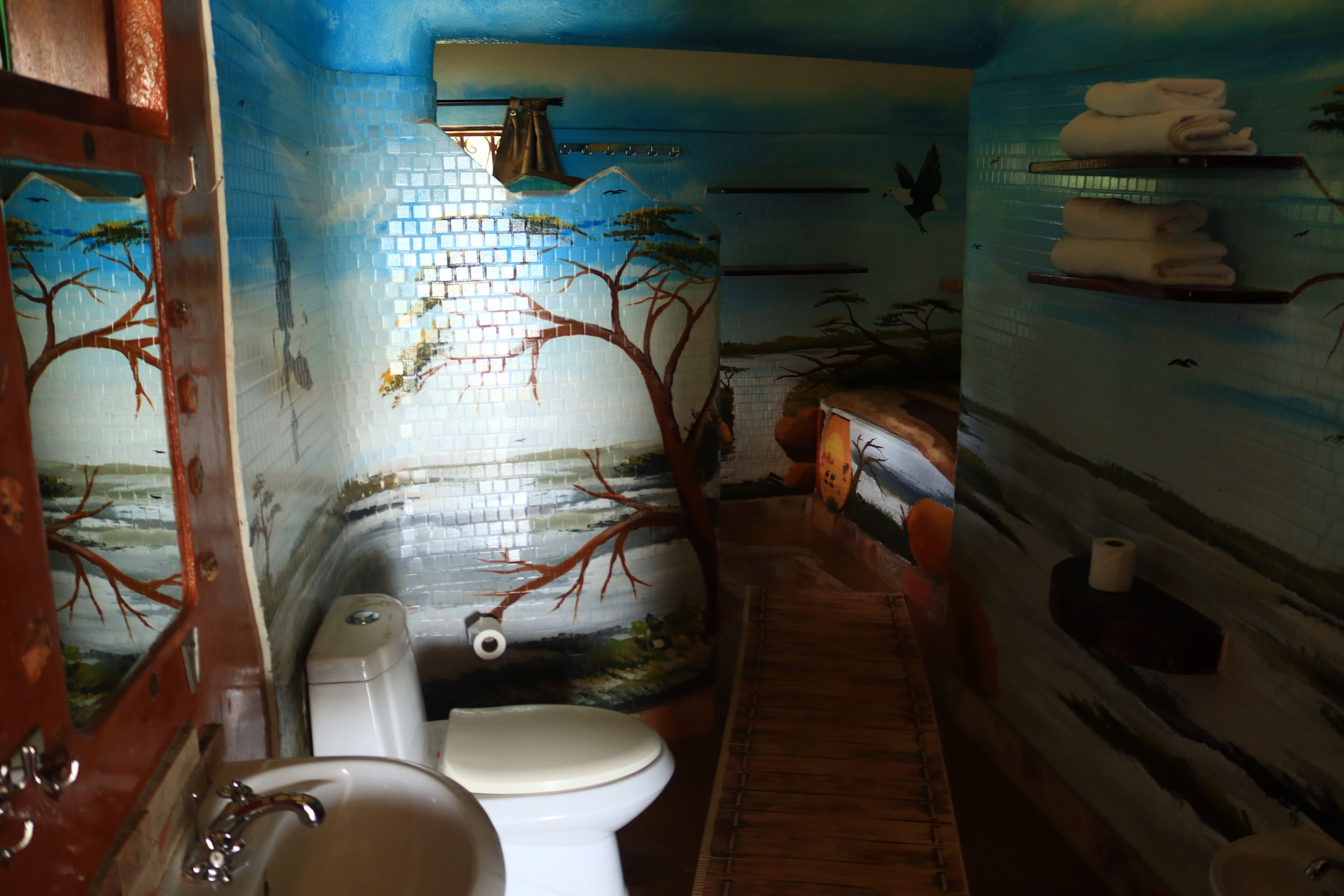 Casa de banho com painel de azulejos, sanita, lavatório e prateleiras com toalhas.