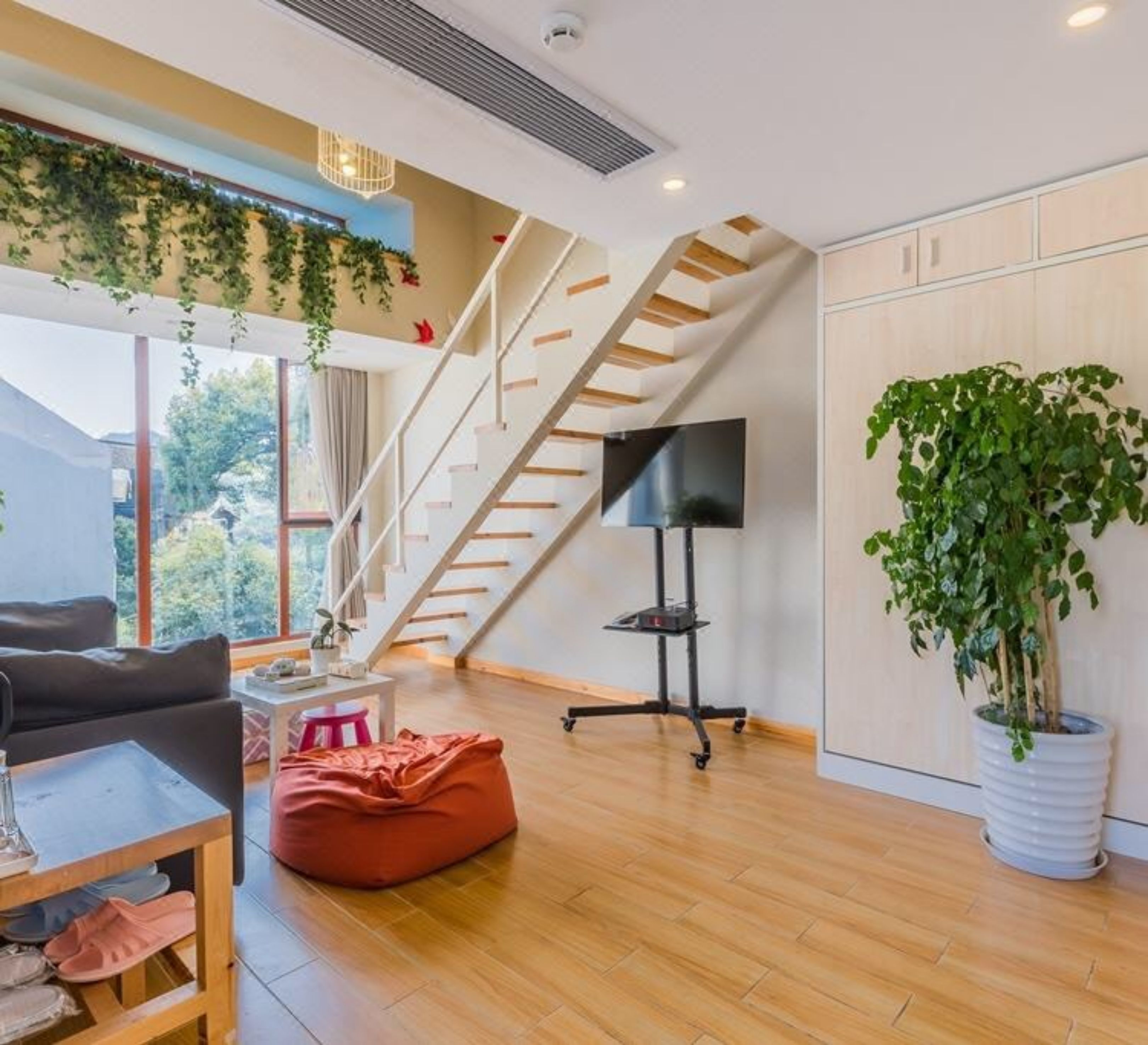 Uma sala de estar moderna com escada de madeira, uma planta grande em vaso e uma televisão de tela plana.