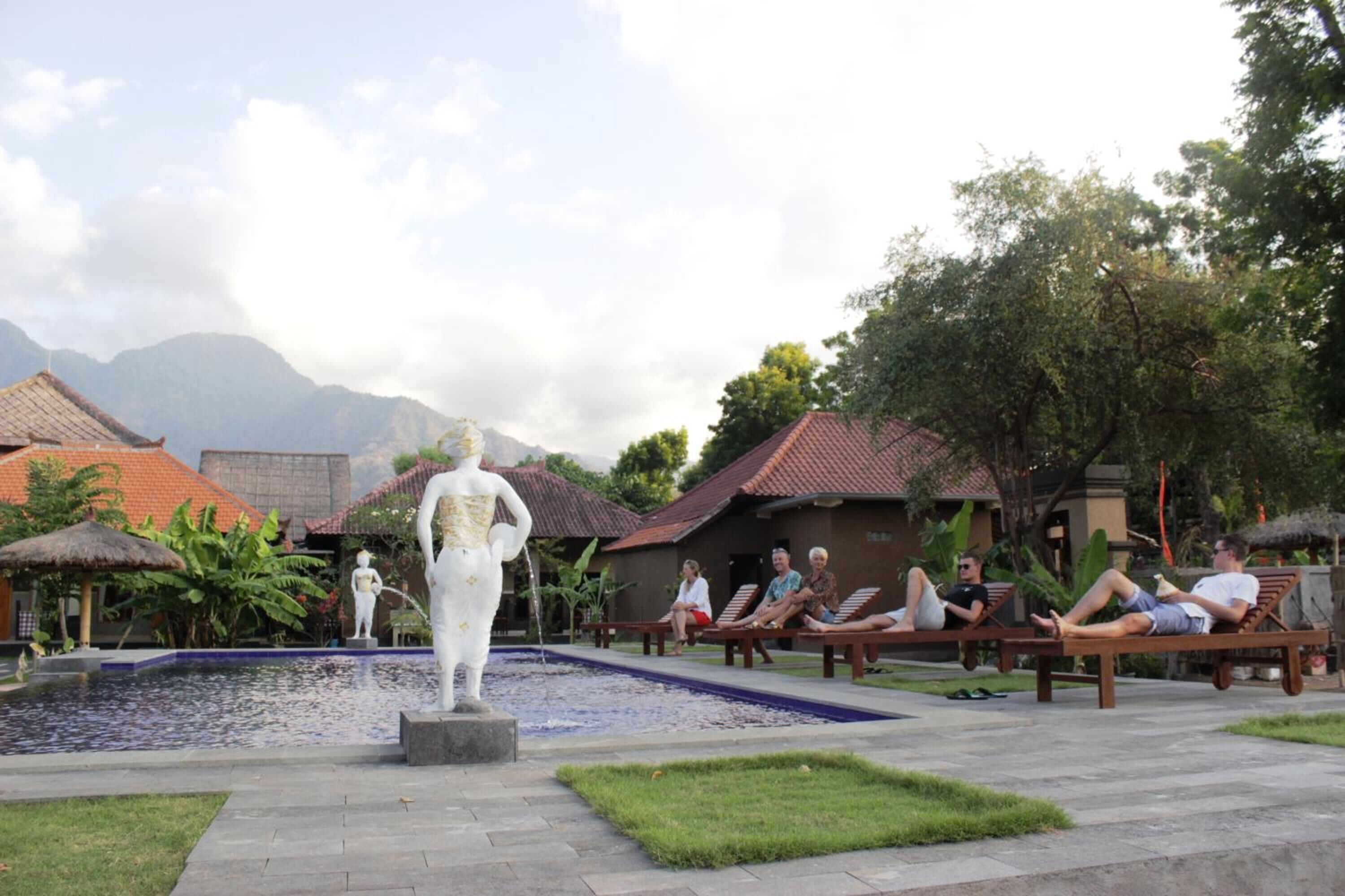 Um pátio com uma estátua, uma piscina e cadeiras de descanso.