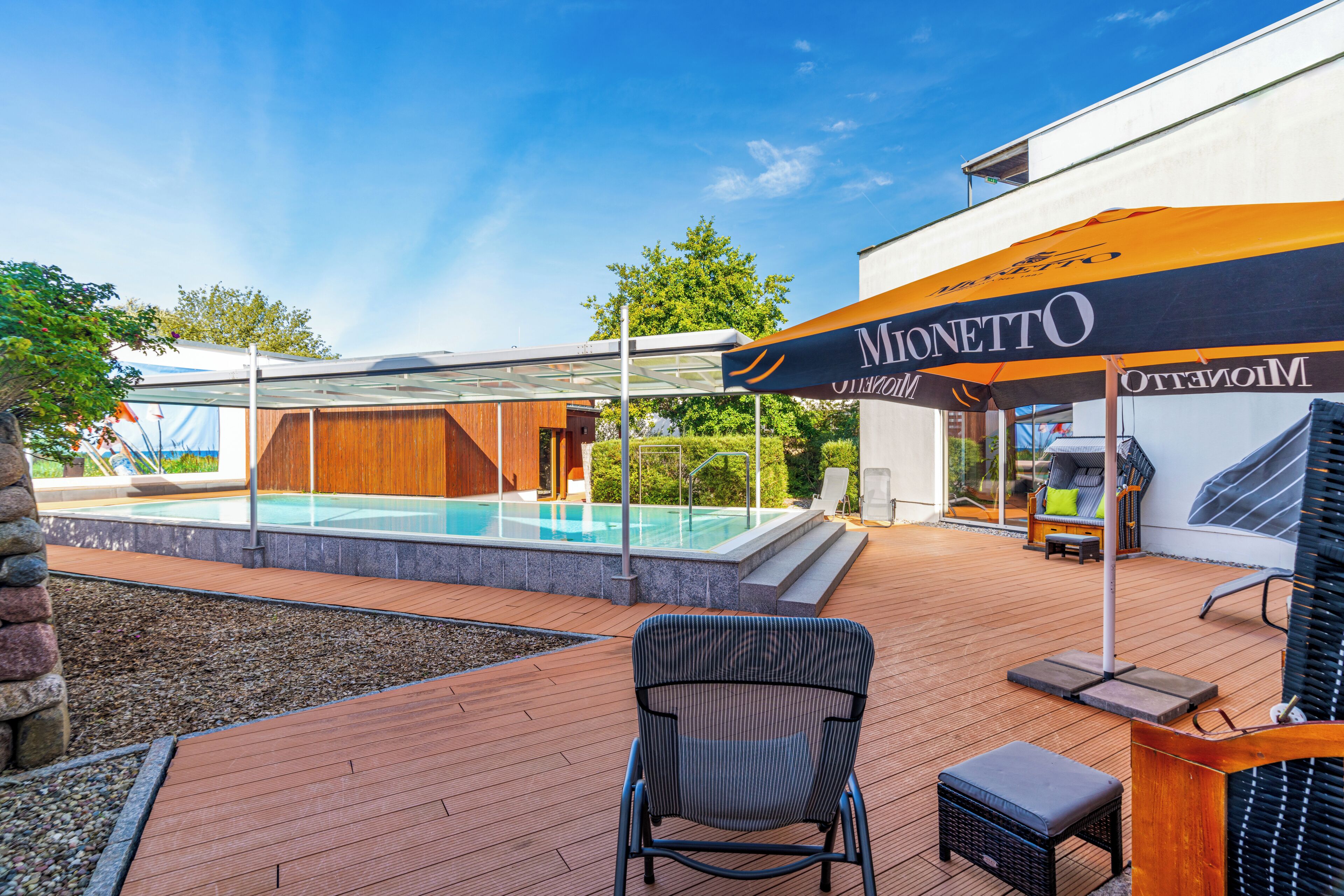 Uma área moderna com piscina ao ar livre, uma espreguiçadeira, um deck de madeira e um espaço para spa com paredes de vidro.