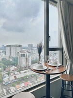 Quarto em arranha-céu com vista para a cidade, mesa redonda com um vaso e janela com cortinas.