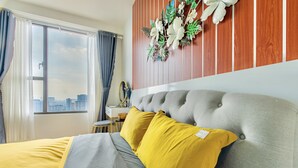 Quarto de hotel com uma cama grande, vista para a cidade, parede de destaque em madeira e uma escrivaninha com cadeira.