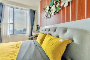 Quarto de hotel com uma cama grande, vista para a cidade, parede de destaque em madeira e uma escrivaninha com cadeira.