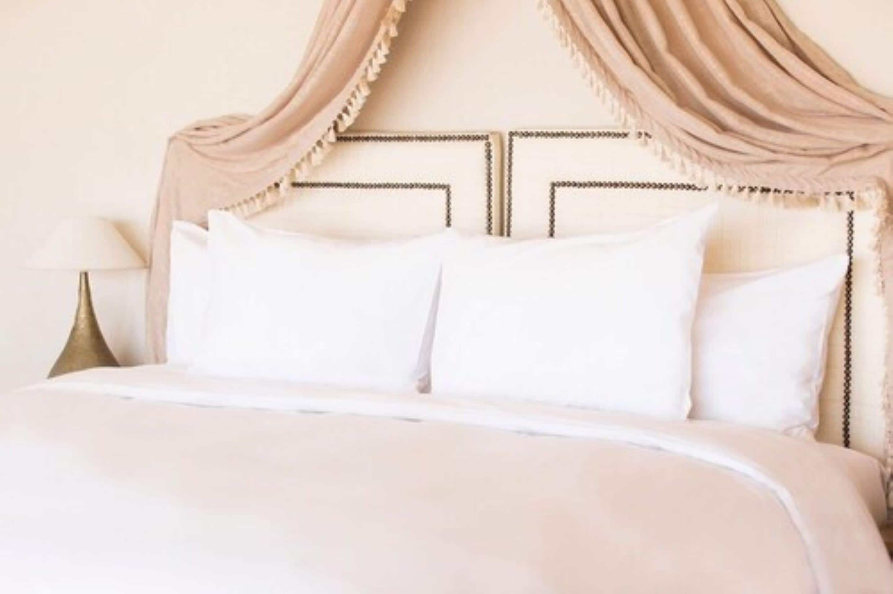 Uma cama com dossel, roupa de cama branca e um abajur ao lado.