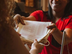 Uma pessoa segurando um papel com texto impresso, possivelmente um recibo de hotel ou pedido de serviço de quarto.