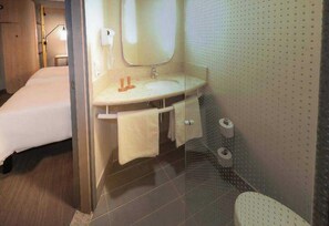 Quarto de hotel com cama, banheiro com pia, espelho, porta-toalhas e vaso sanitário.