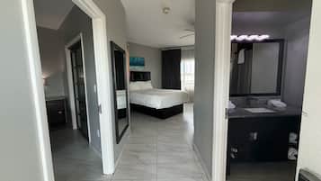 Quarto de hotel moderno com cama, um espelho grande, banheiro com pia e vista para o exterior.