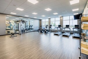 Uma academia ampla com esteiras, aparelhos de musculação e um painel de espelhos.