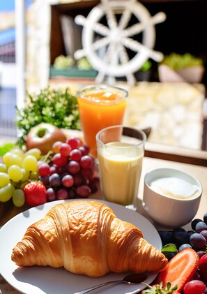Uma mesa posta para o pequeno-almoço, com um croissant, fruta, sumo e leite.