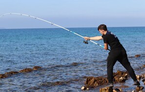 Uma pessoa pescando no mar com uma vara de pesca comprida.