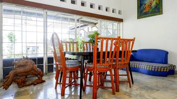Uma área de refeições com mesa e cadeiras, um sofá azul e uma janela grande com vista para o exterior.
