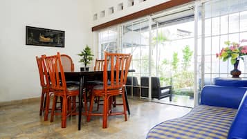 Uma área de refeições com mesa e cadeiras, uma planta em vaso e um sofá com almofada estampada.