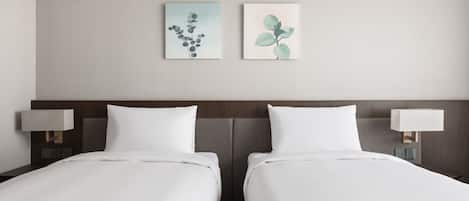 Quarto de hotel com duas camas, cabeceira, abajures e duas obras de arte penduradas na parede.