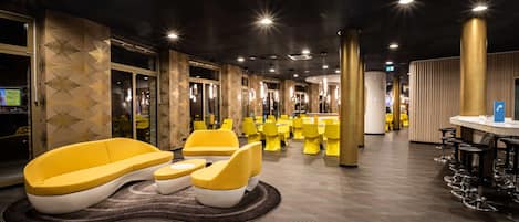 Um saguão de hotel moderno com assentos amarelos, área de bar e paredes estampadas.