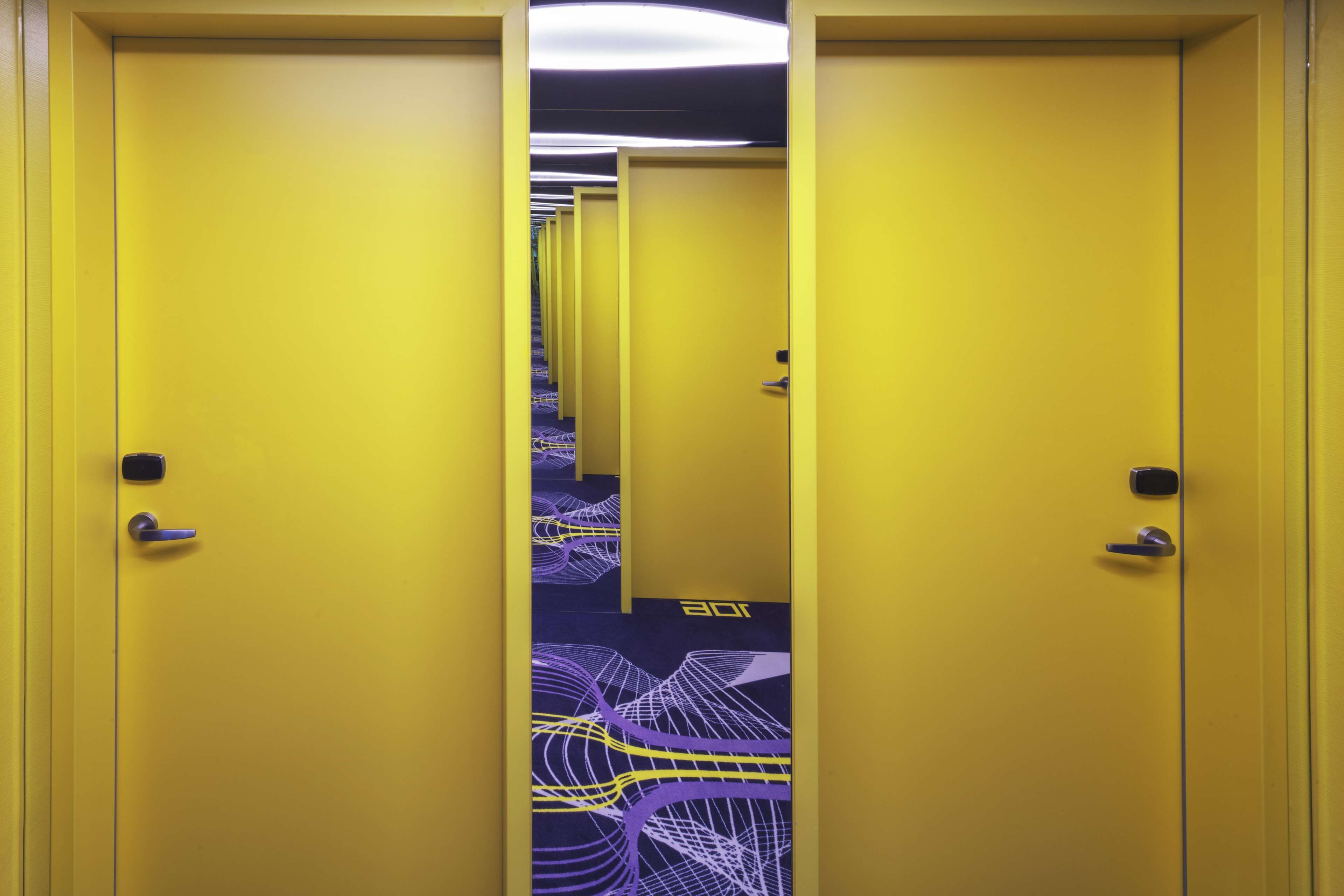 Um corredor com portas amarelas e um tapete roxo com linhas amarelas.