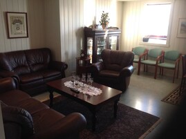 Uma sala de estar com um sofá de couro marrom escuro, uma mesa de centro de madeira com um sousplat de renda, um armário de vidro e uma janela com cortinas.