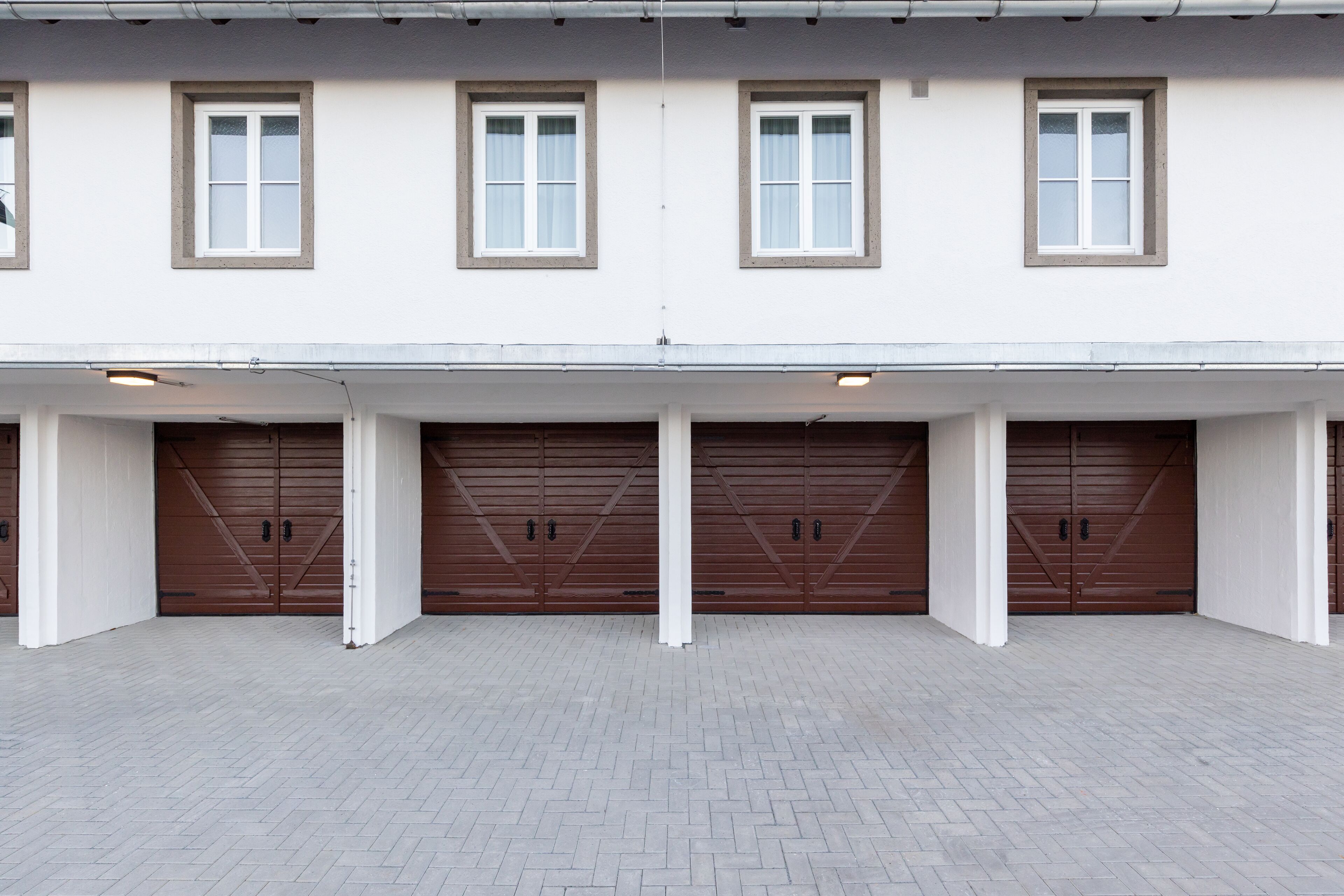 Um edifício com quatro grandes portões de garagem, um telhado plano e uma área de entrada pavimentada.