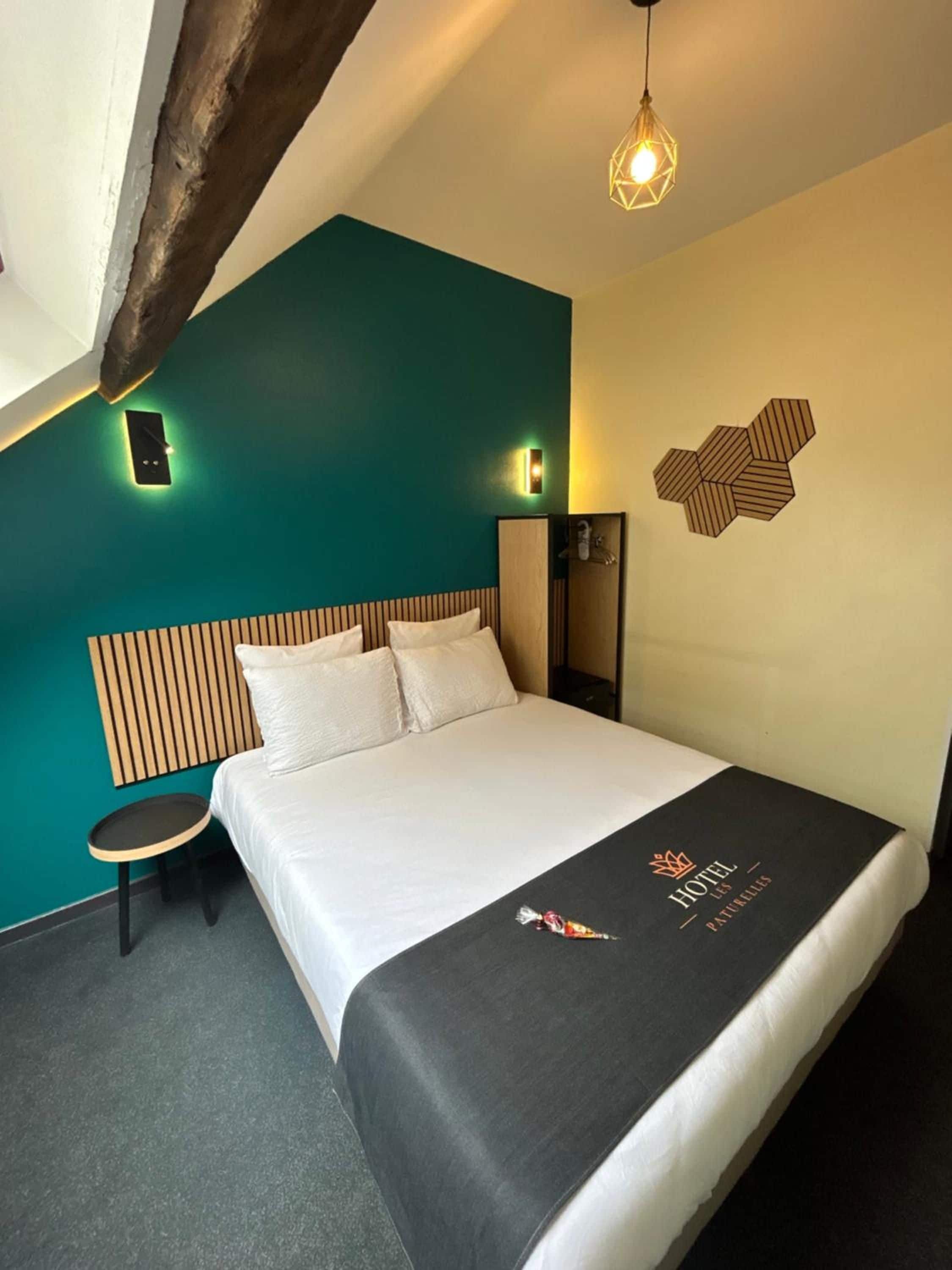 Quarto de hotel com cama, mesa de cabeceira, luminária na parede e um objeto decorativo na parede.