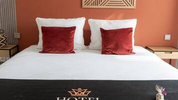 Quarto de hotel com uma cama, duas almofadas, um objeto decorativo na parede e um espalha-cama preto com o nome do hotel.