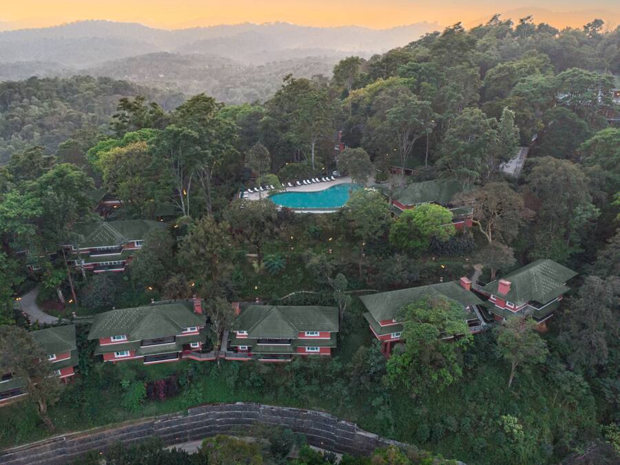 Vista aérea de um resort com vários edifícios tipo bangalô, uma piscina e vegetação exuberante ao redor.
