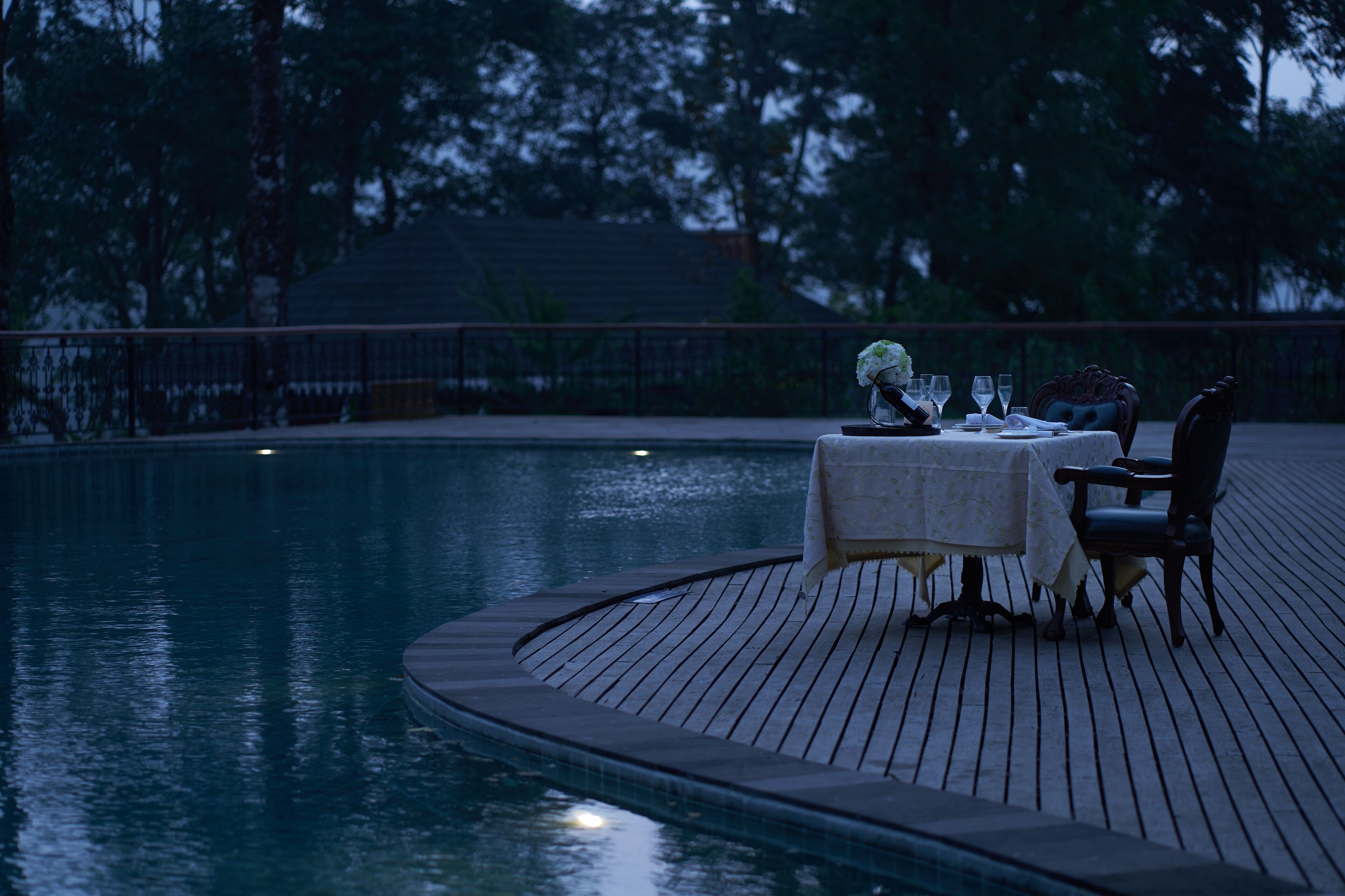 Espaço de refeições com mesa e cadeiras perto de uma piscina, rodeado por um deck de madeira e guarda-corpo.