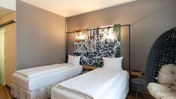 Quarto de hotel com duas camas de solteiro, uma grande obra de arte abstrata na parede, uma pequena mesa redonda e uma cadeira preta distinta.