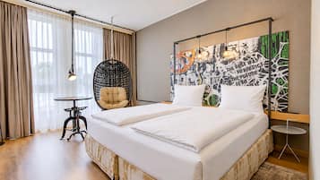 Quarto de hotel com cama grande, cadeira suspensa, mesa pequena e parede com pintura de paisagem urbana.