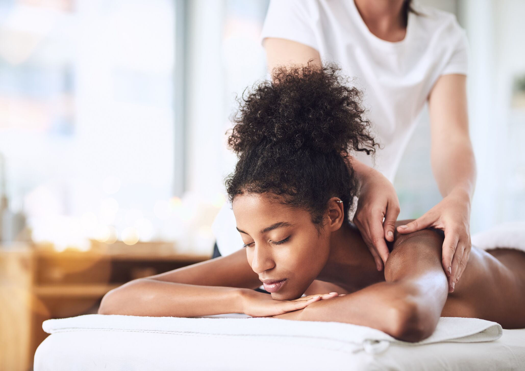 Uma pessoa recebendo massagem em um quarto com uma janela grande e uma cama branca.