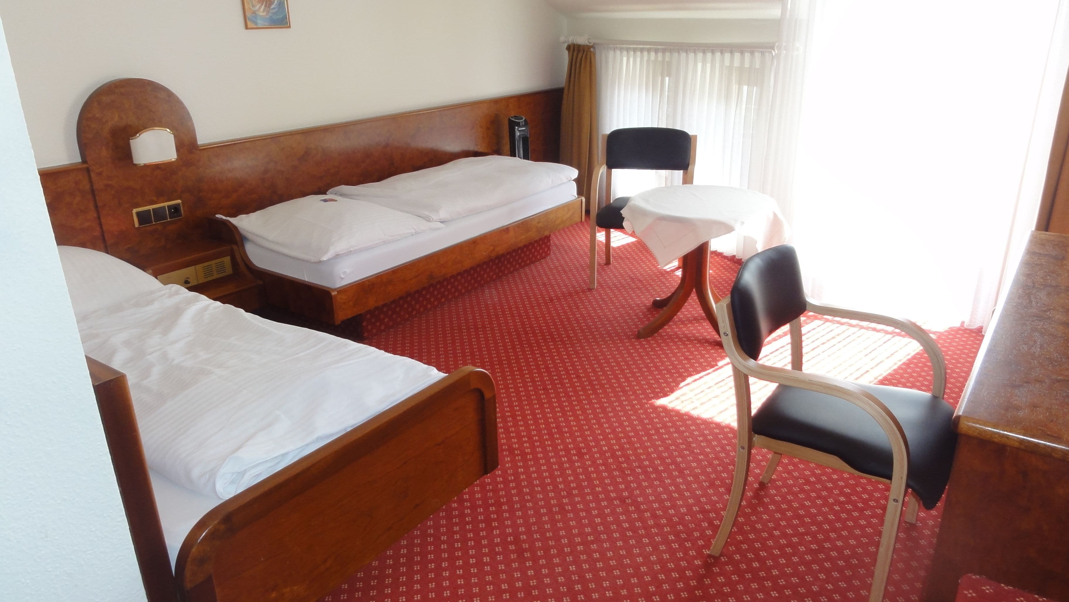 Quarto de hotel com duas camas de solteiro, uma mesinha com uma cadeira e uma janela com cortinas.