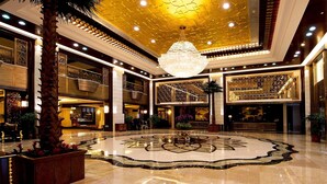 Um hall espaçoso com um grande lustre ornamentado, piso de mármore polido e uma fonte decorativa central.