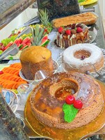 Diversos doces, incluindo um bolo de chocolate com cerejas e folhas de hortelã, um bolo bundt e um bolo com cobertura branca e morangos.