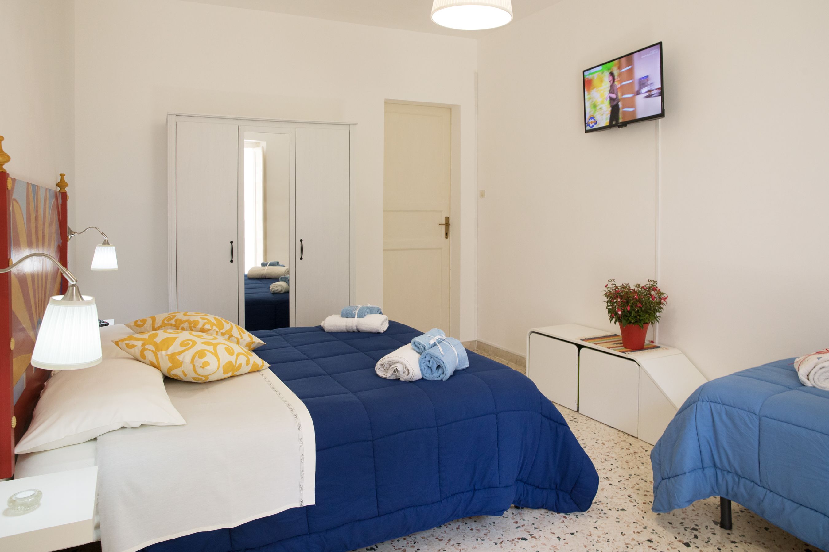 Quarto de hotel com cama, mesa de cabeceira, luminária, televisão e porta.