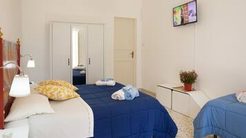 Quarto de hotel com cama, mesa de cabeceira, luminária, televisão e porta.