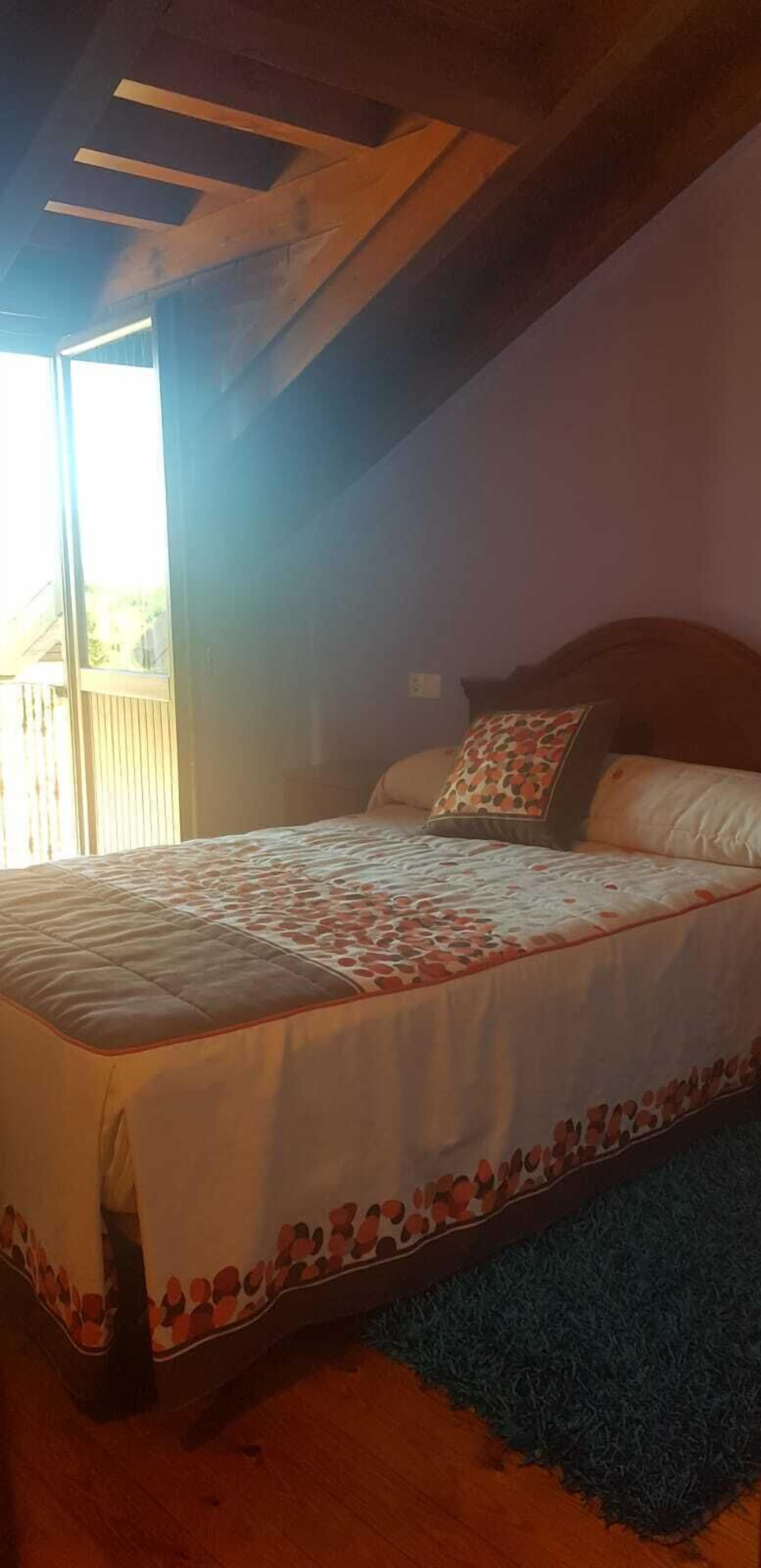 Quarto com cama, teto de madeira e vista para o exterior.