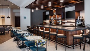 Uma área de bar moderna com balcão de madeira, assentos com cadeiras estampadas e uma grande televisão de tela plana sobre o balcão.