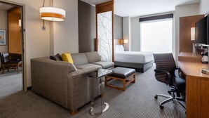 Quarto de hotel com sofá, mesa pequena, escrivaninha, cadeira, cama e televisão.