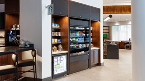 Um saguão de hotel moderno, com um balcão da Starbucks, exposição refrigerada de bebidas e área de estar.