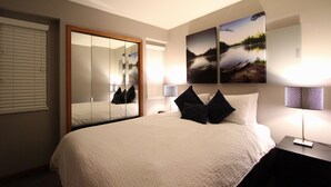 Quarto de hotel com uma cama grande, um espelho e dois quadros pendurados na parede.