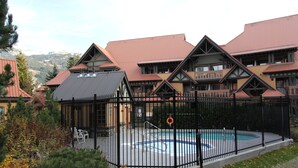 Área de piscina cercada por uma grade preta, com um flutuador salva-vidas, ao redor de edifícios com vista para uma montanha ao fundo.