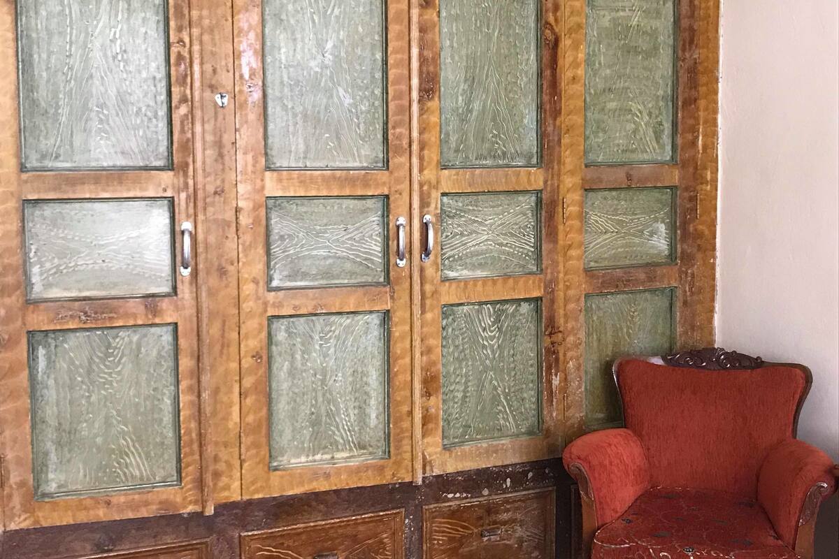 Um armário de madeira com portas de vidro e puxadores, uma poltrona estofada vermelha e um armário abaixo.