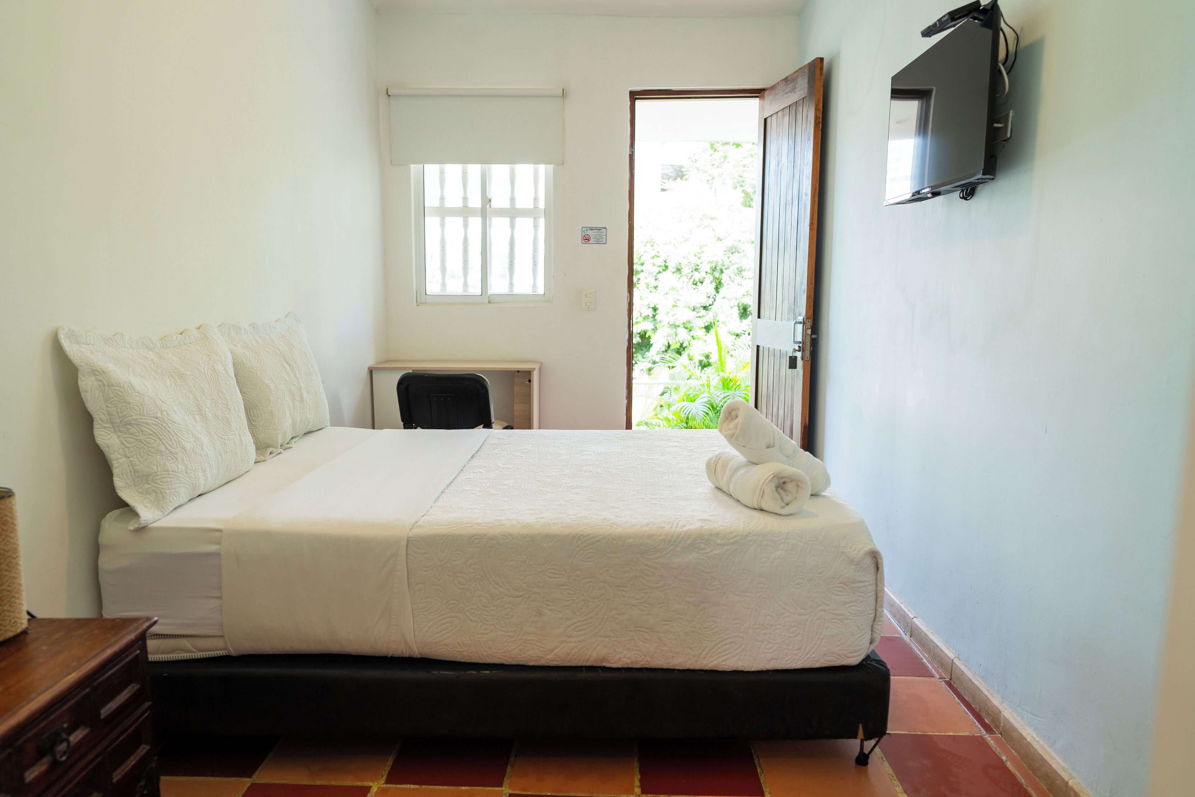 Quarto com cama, escrivaninha e televisão.