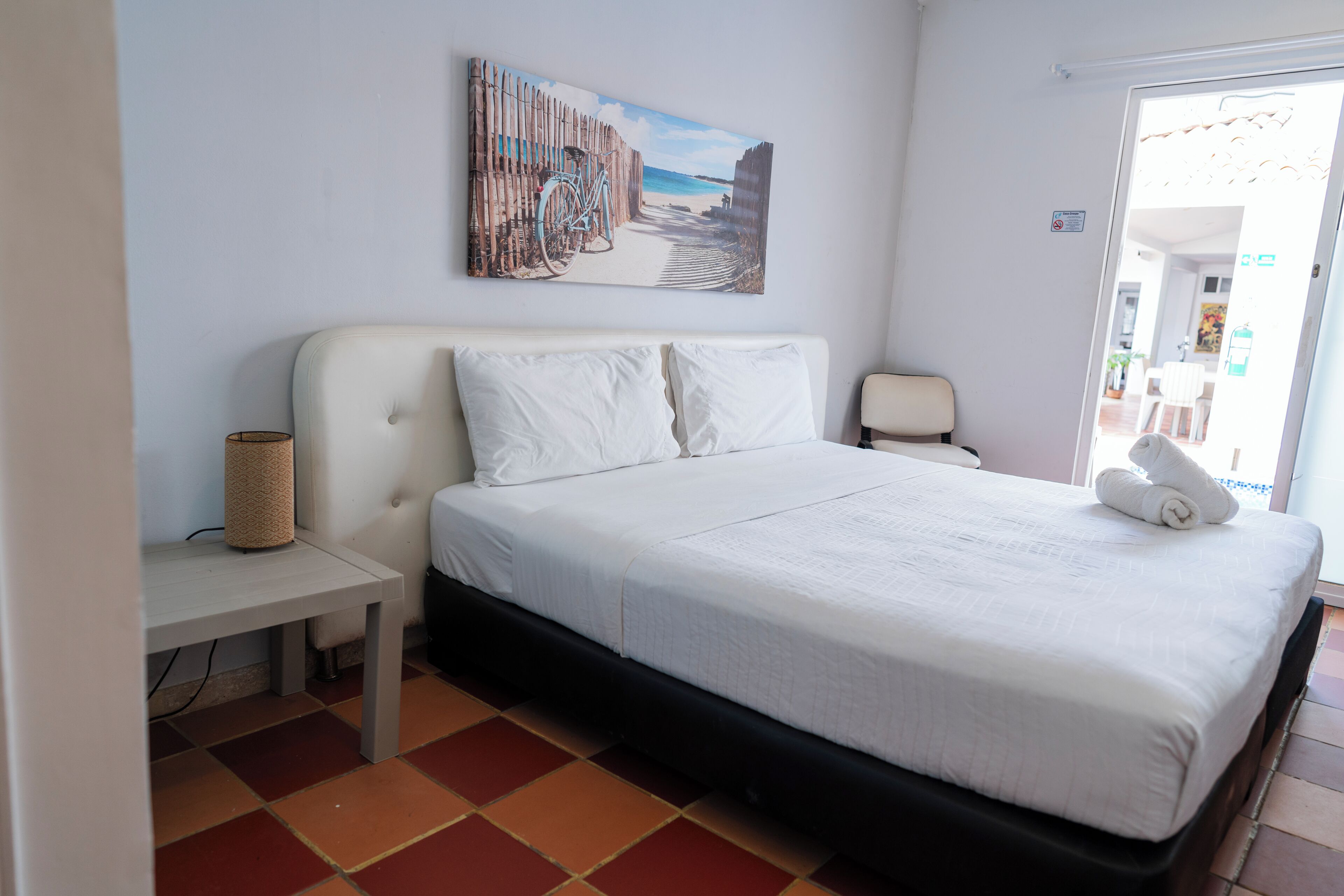 Quarto com cama, mesa de cabeceira, cadeira e um quadro na parede.