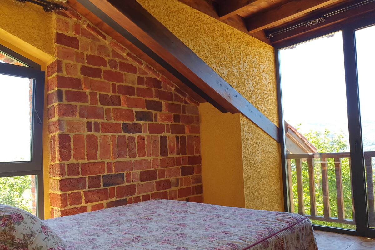 Quarto com parede de tijolos, viga de madeira e varanda com guarda-corpo.