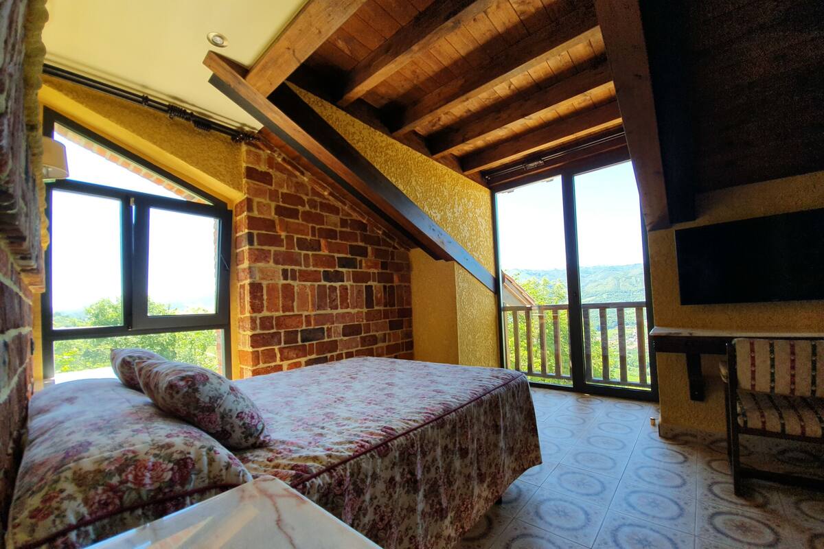 Quarto com cama, sofá, televisão e varanda com vista para o campo.