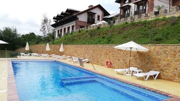 Uma piscina com espreguiçadeiras e guarda-sóis, rodeada por muros de pedra e edifícios.