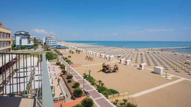 Uma praia com fileiras de espreguiçadeiras e guarda-sóis, um parquinho e vista para o mar.