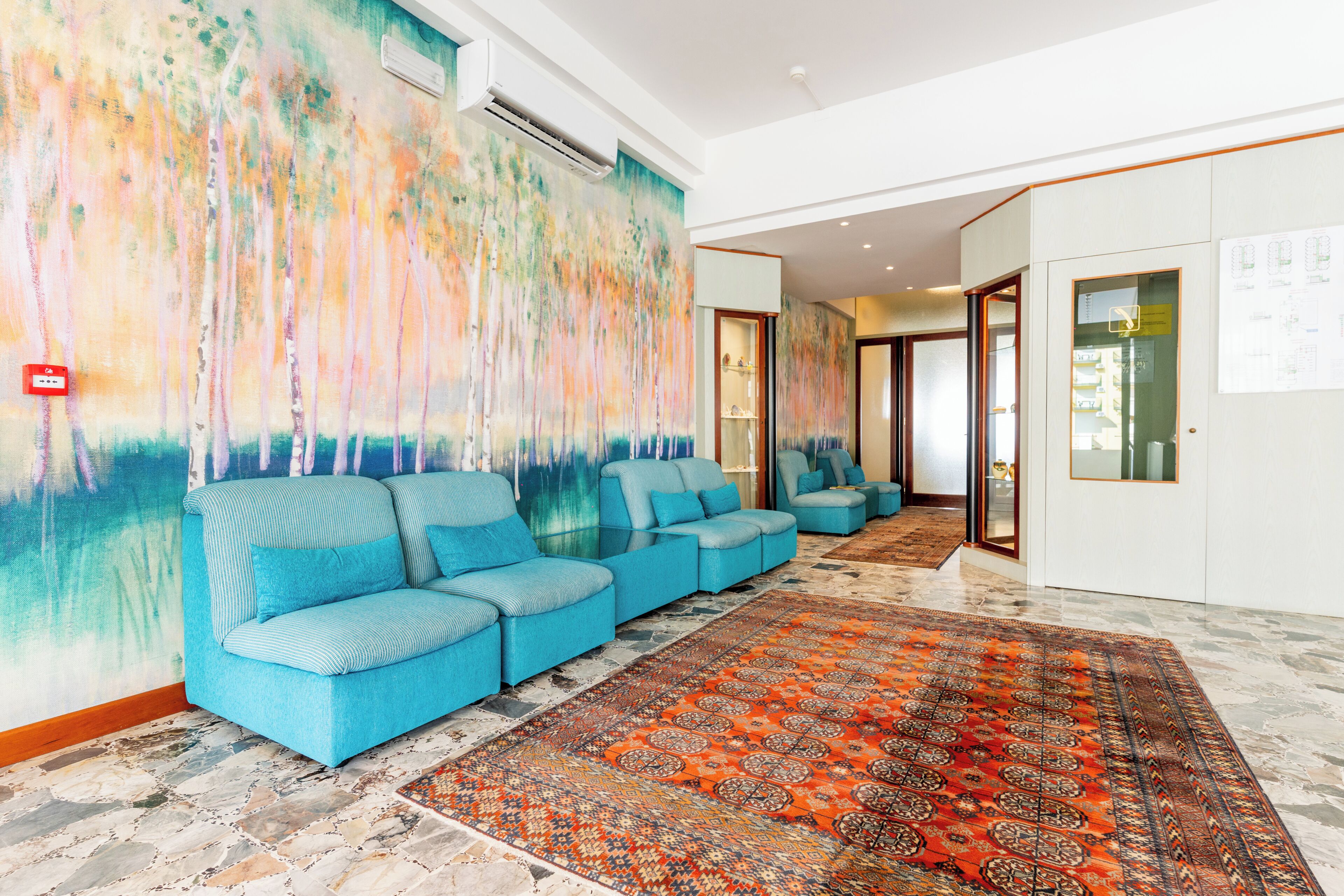 Um hall moderno com um sofá azul, um tapete estampado e um grande quadro abstrato na parede.
