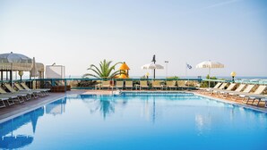 Piscina com espreguiçadeiras e guarda-sóis, uma palmeira e um edifício com cúpula e torre.